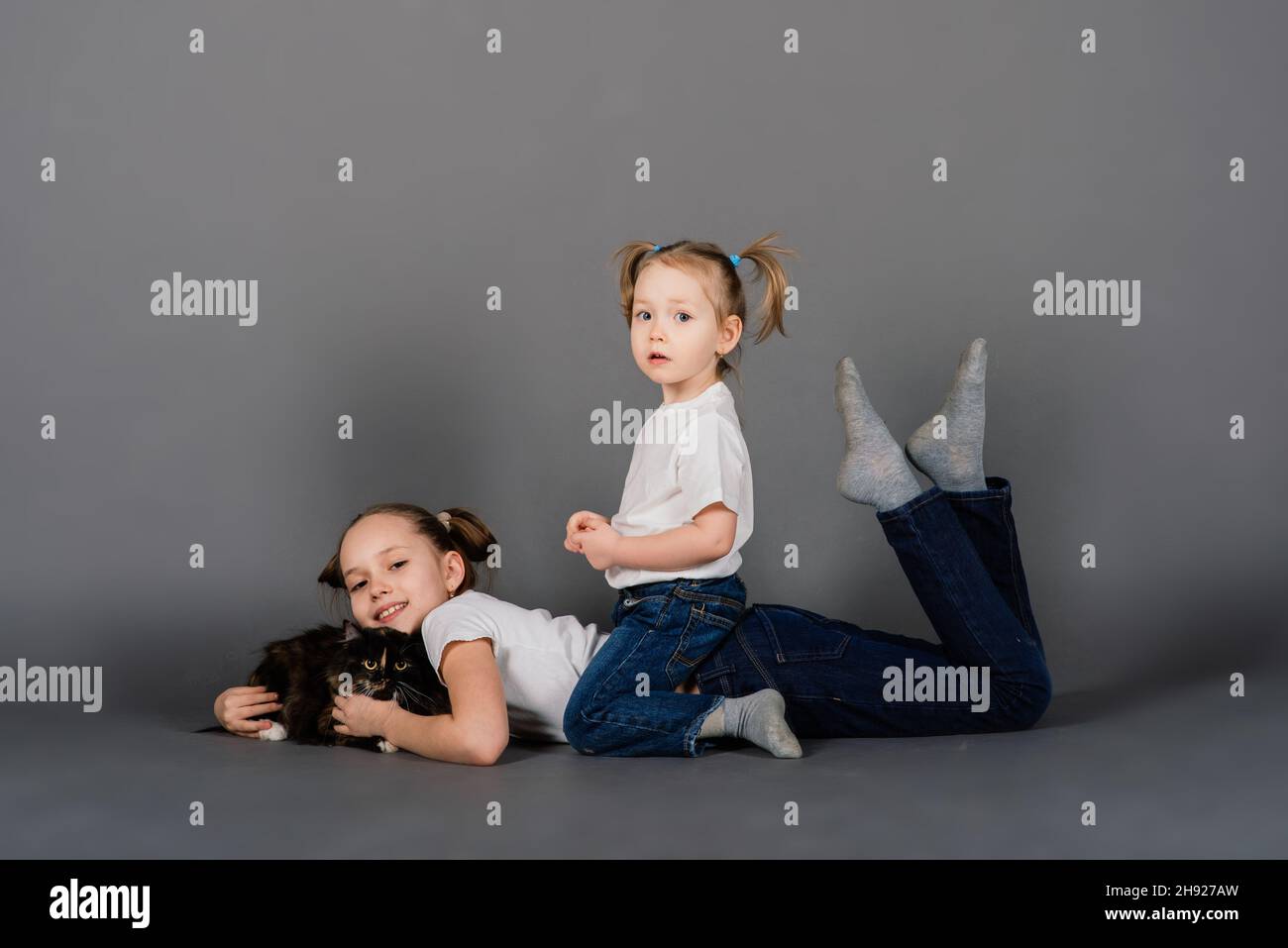 Two girls sisters hugging black cat in a studio Stock Photo - Alamy