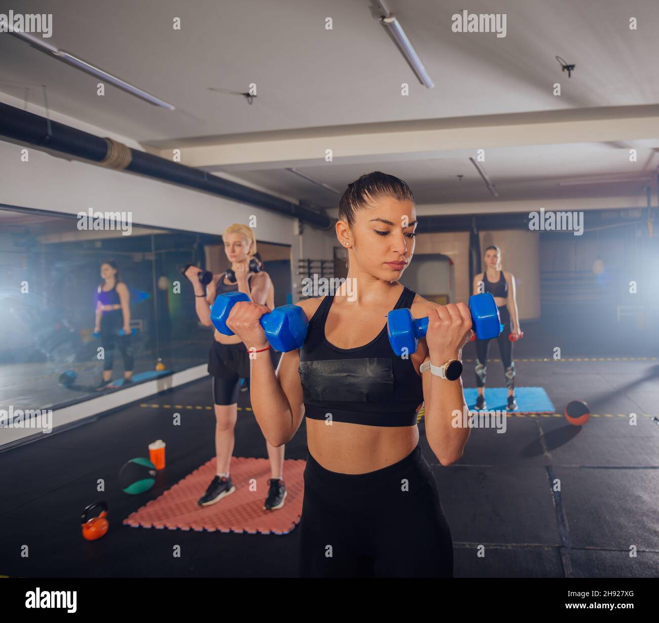 Group of athletic young women in sportswear with dumbbells exercising ...