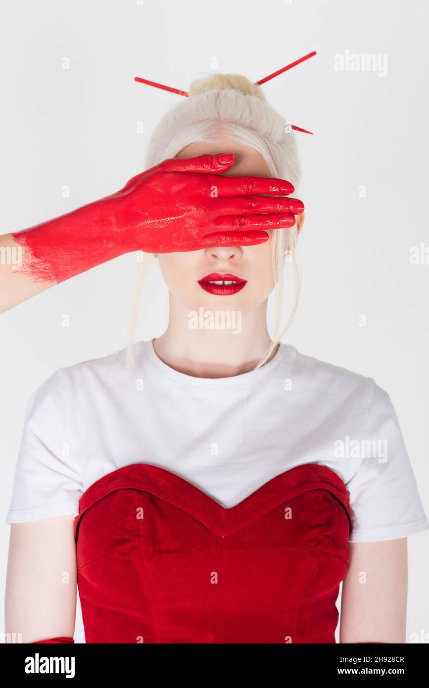 Woman with red paint on hand covering eyes of blonde model isolated on ...