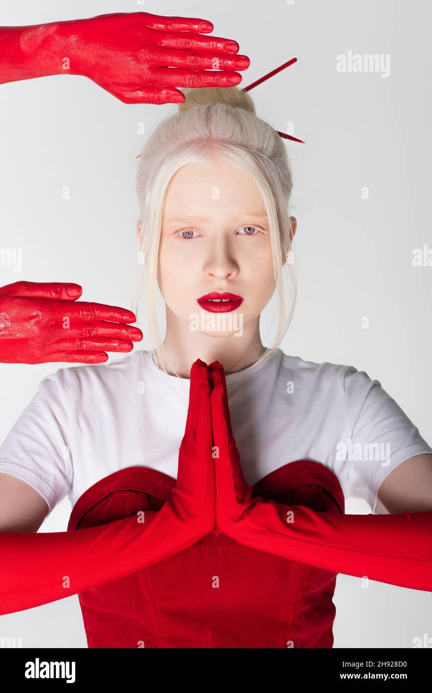 Stylish albino model in gloves showing praying hands near female hands ...