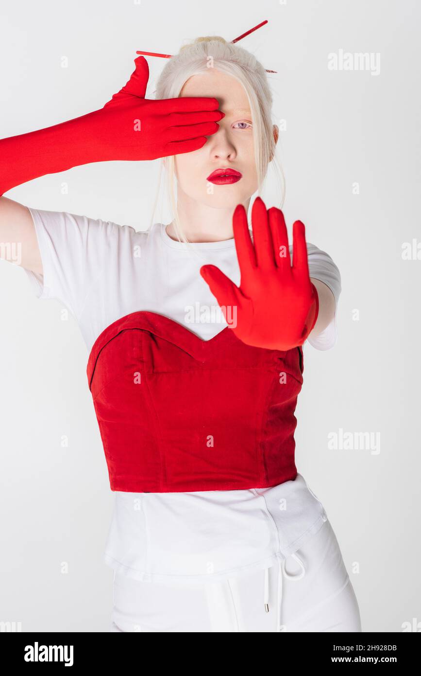 Trendy albino model in gloves and red lips showing stop gesture ...