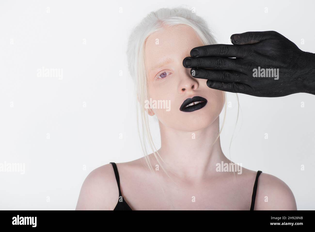 Male hand in black paint covering eye of albino woman isolated on white ...