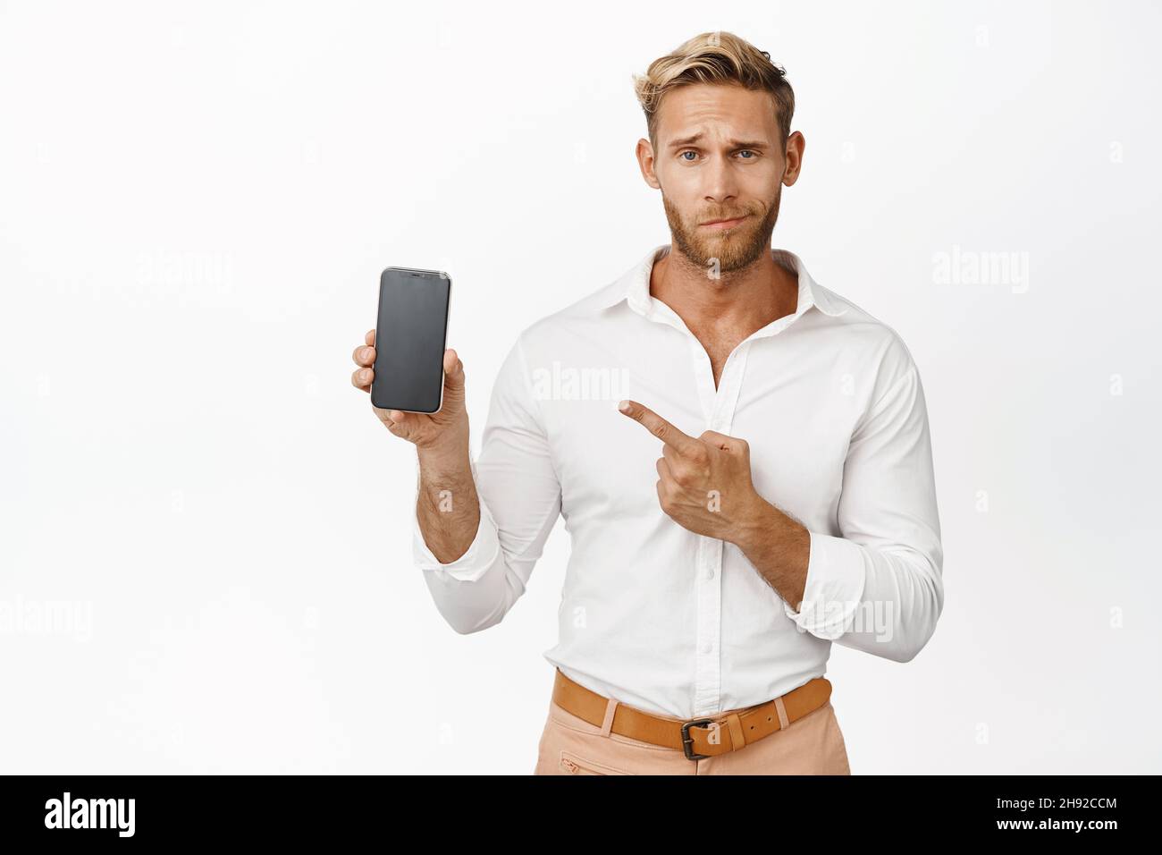 Portrait of smiling macho man pointing at his phone with smug face ...