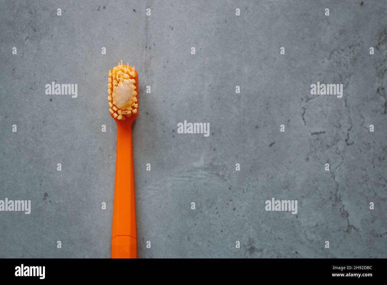 Orange plastic toothbrush with toothpaste on gray concrete table ...