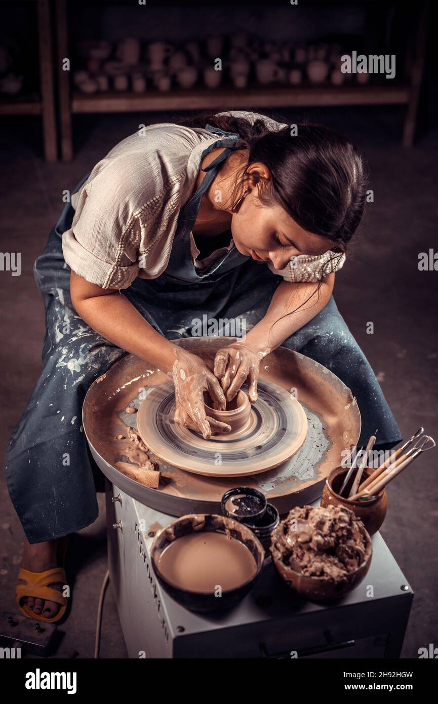 Beautiful artisan girl making pottery, sculptor from wet clay on wheel ...