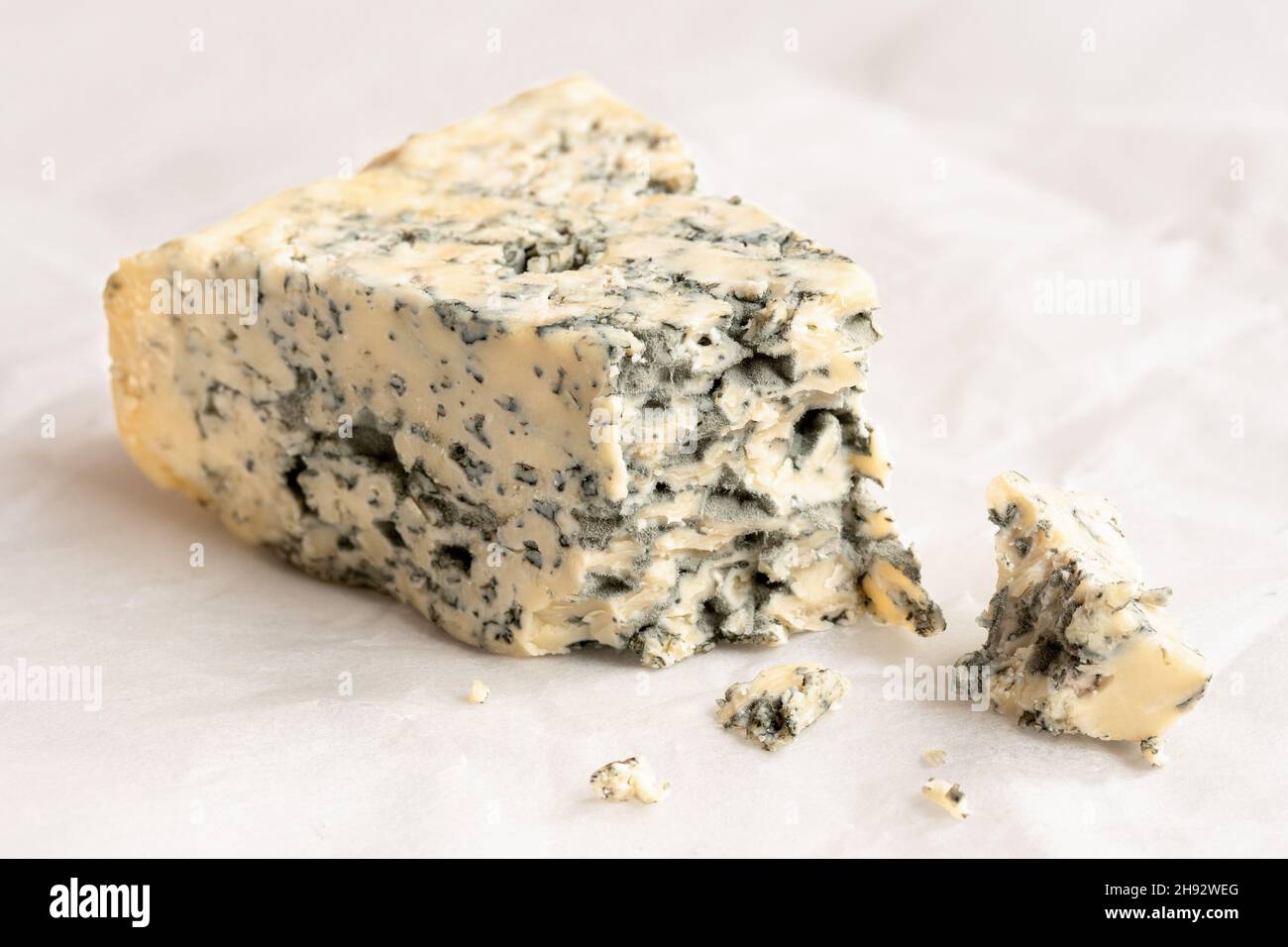 Broken blue cheese wedge with crumbles on wax paper Stock Photo - Alamy