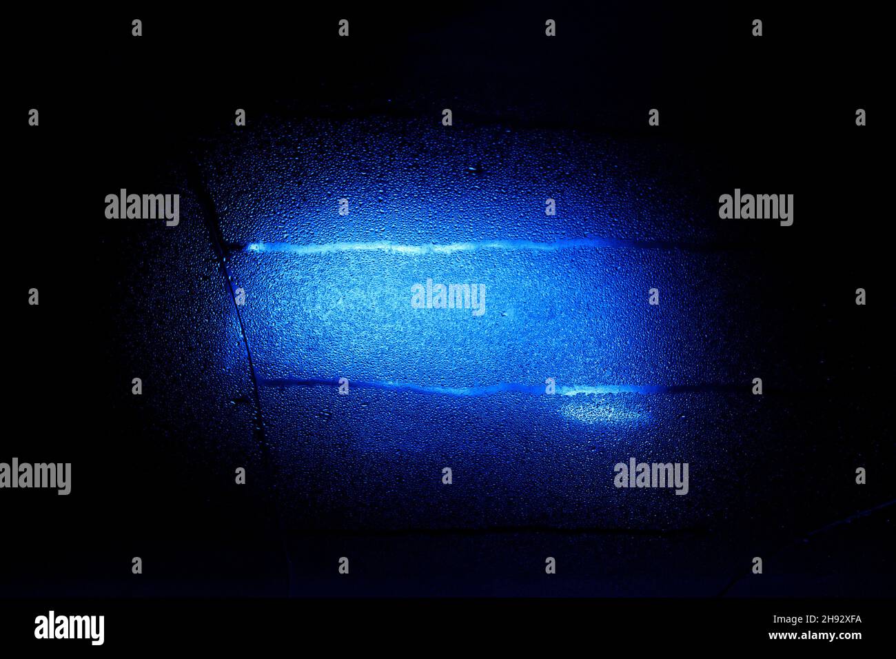 A blue spot of light through old glass in the dark on a black ...