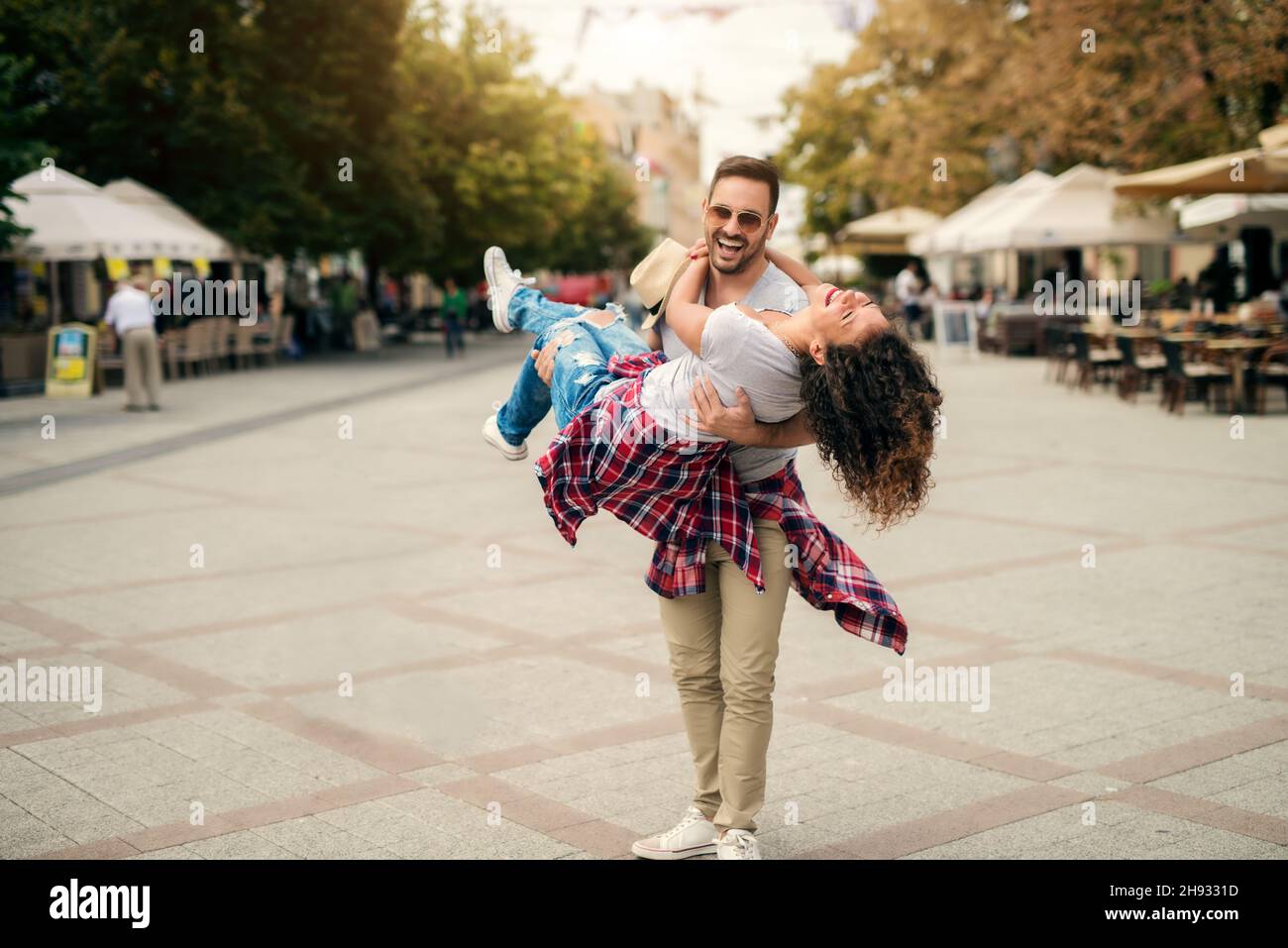 Happy couple enjoys at streets of the city. He is holding her spinning ...