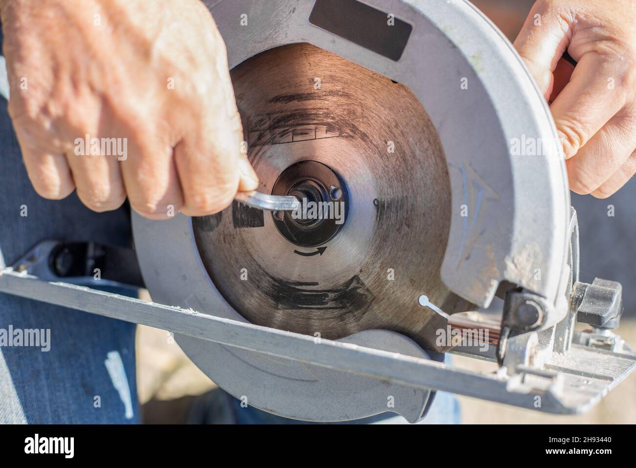 man screws a saw blade with a hexagon to an electric miter saw for ...