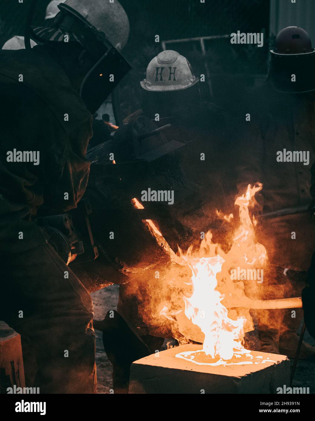 Vertical shot of adult industrial workers in uniforms melting metal in ...