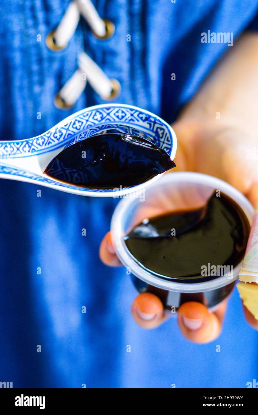 Woman hand spoons up the black jelly snack called Guiling Gao, a ...