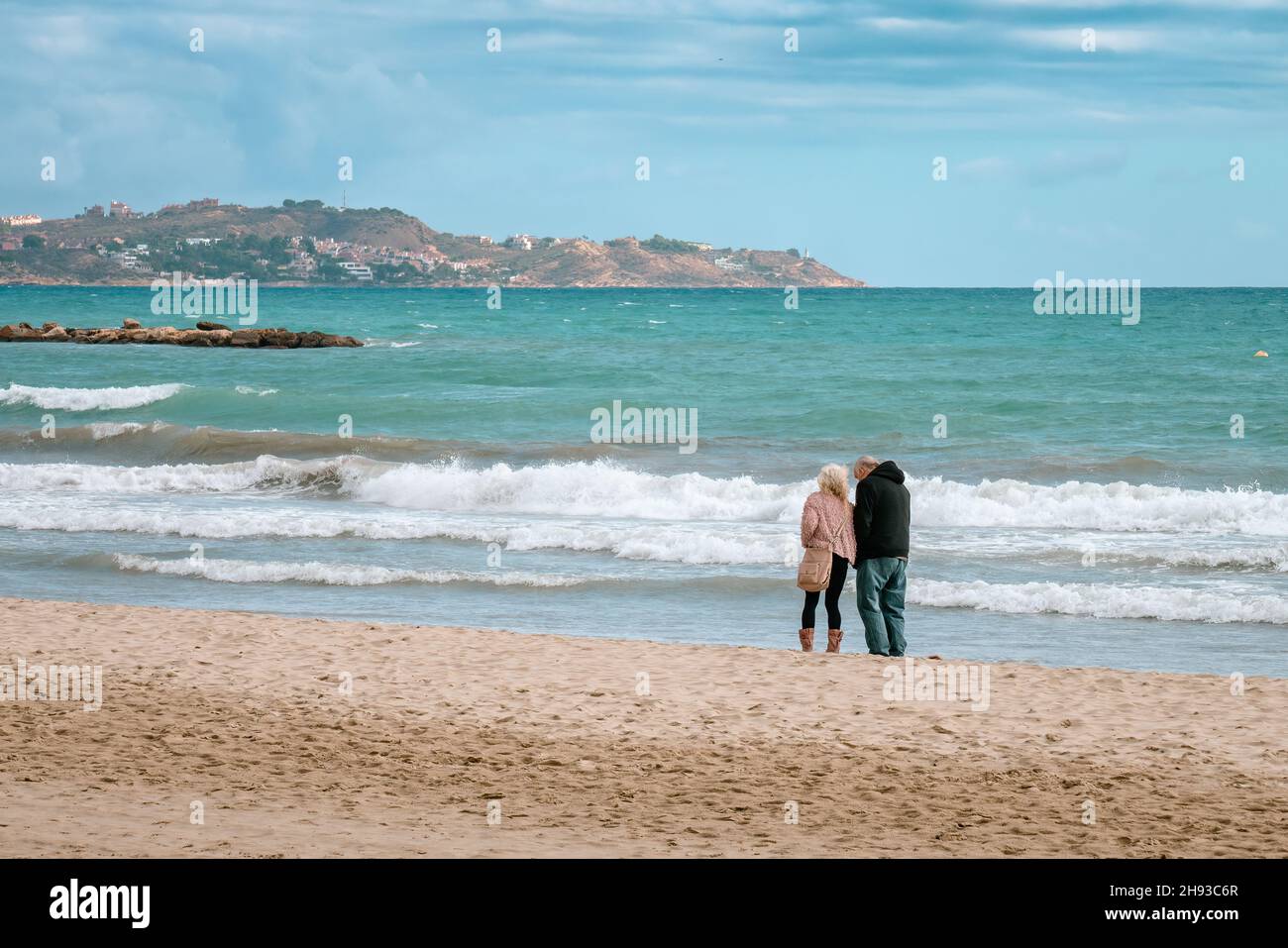 Older pair looking at something at shore line on winter beach in ...