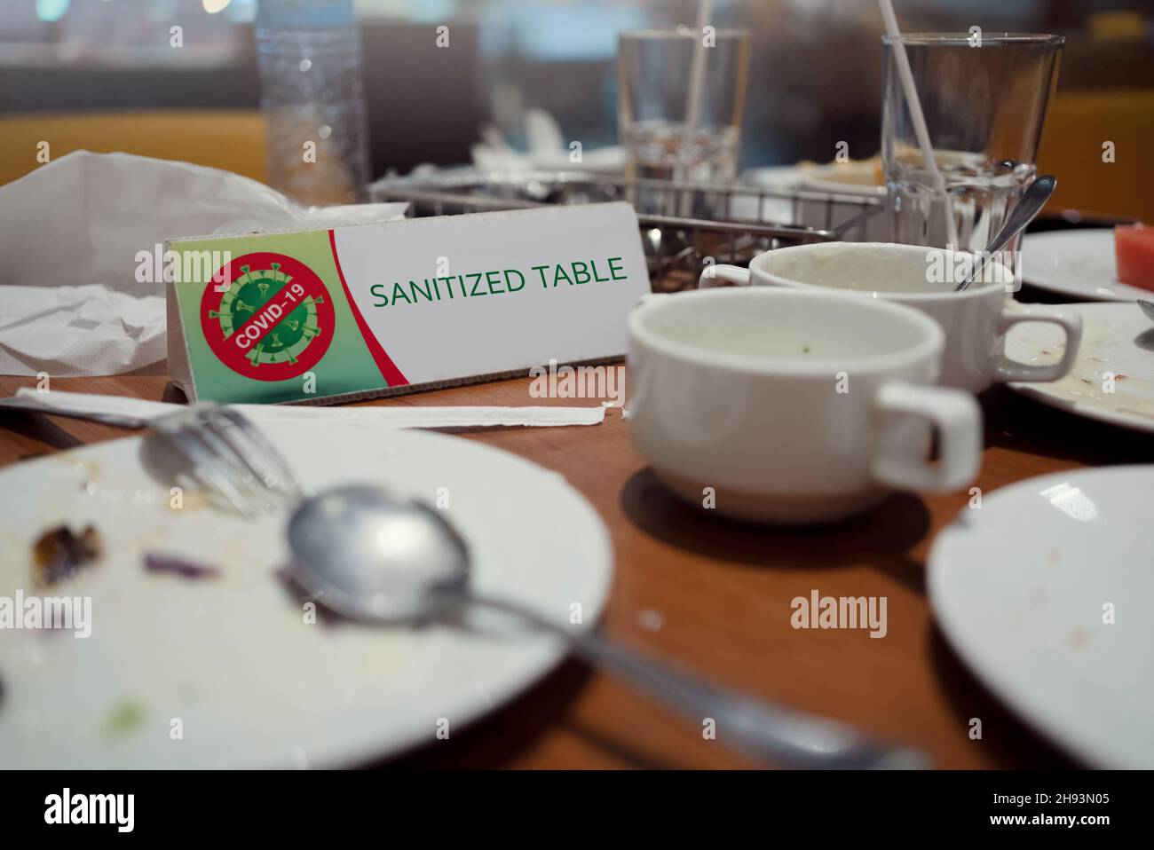 Empty dishes on the dining table with sanitized table sign in a ...