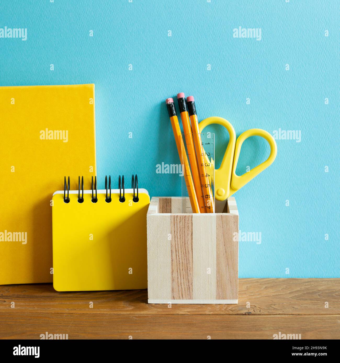 Yellow notebook, pencil holder, scissor, ruler on wooden desk. blue ...