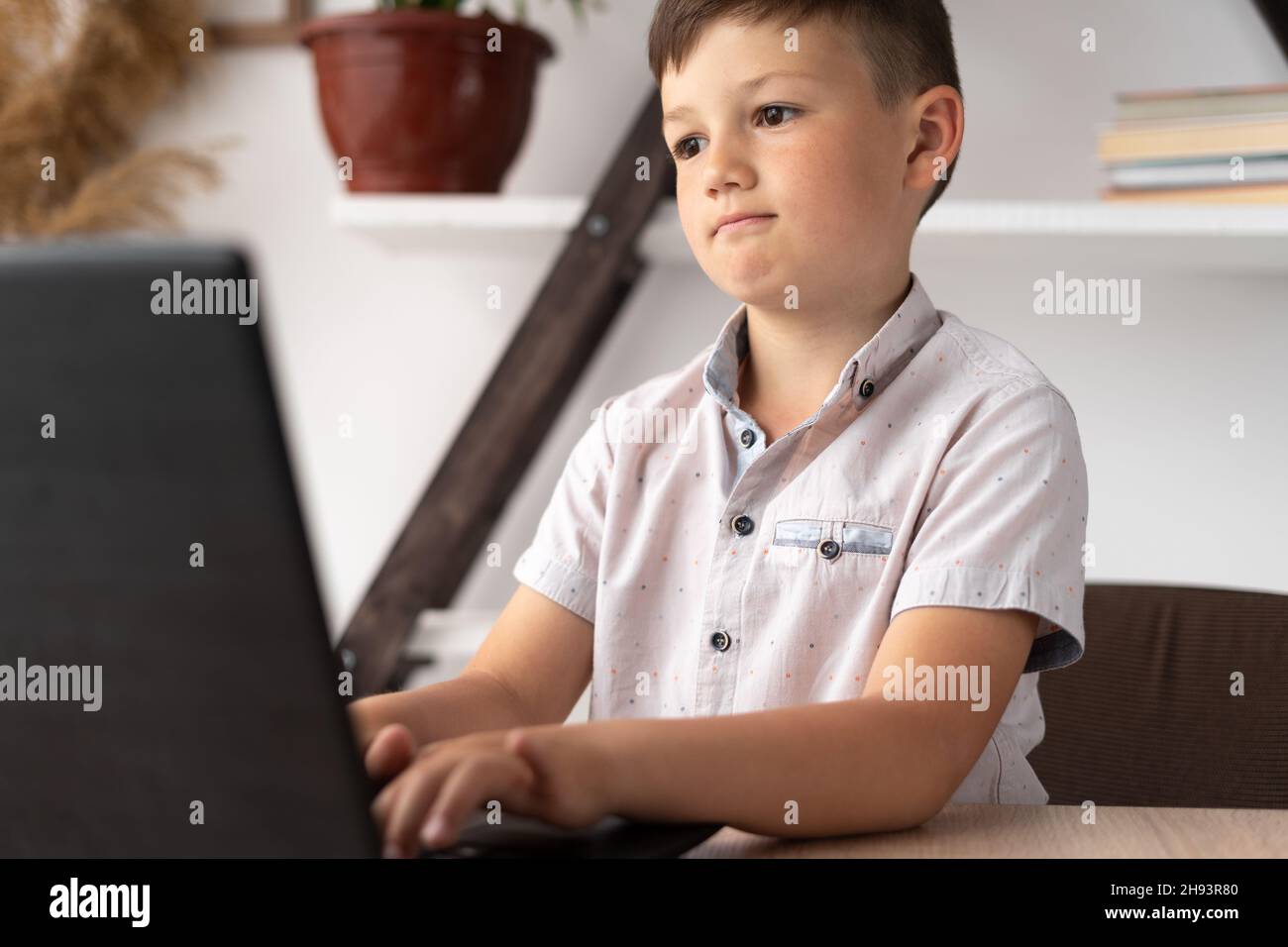 Portrait of a concentrated schoolboy typing on the keyboard of a laptop ...