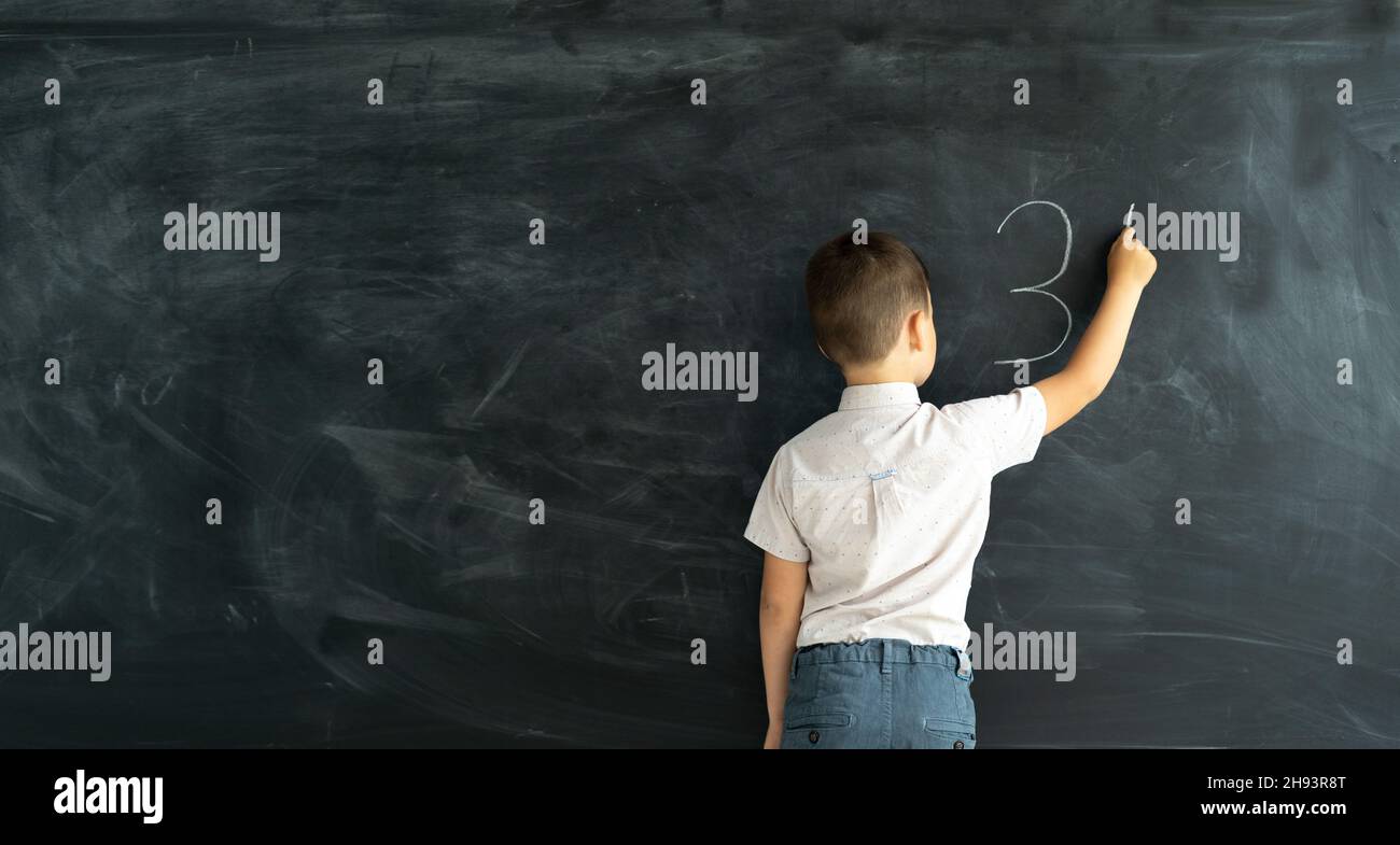Pupil in class at a math lesson writes on a chalk board with chalk ...