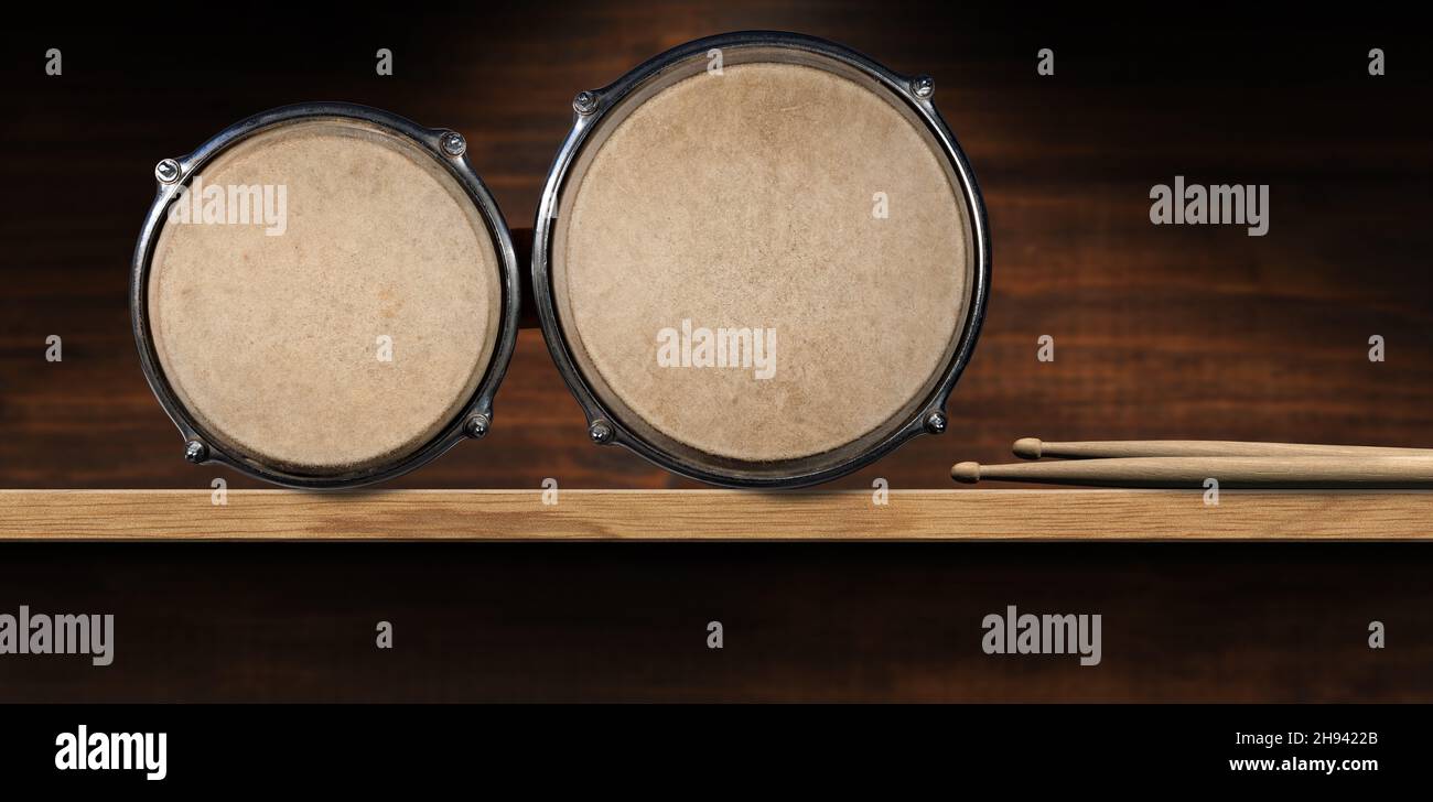Close-up of bongo drums and a pair of drumsticks, above a wooden shelf ...