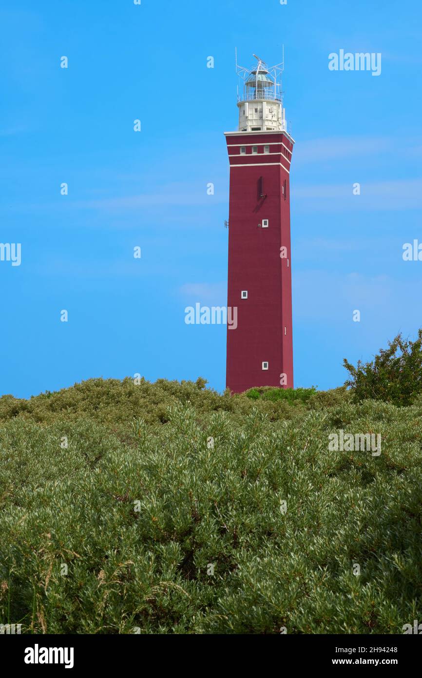 Red lighthouse, square tower, in front of green bushes, blue sky in the ...