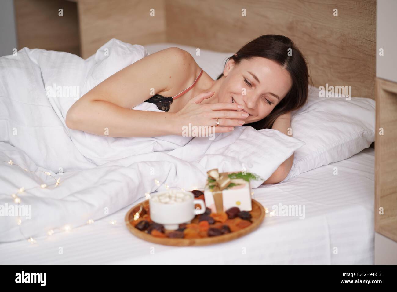 Woman awake on the bed with present and coffee with marshmallows ...