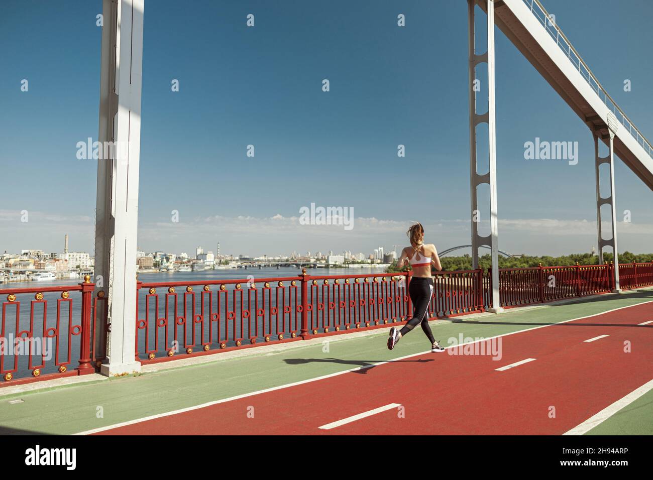 Woman trains running along road on contemporary footbridge on summer ...