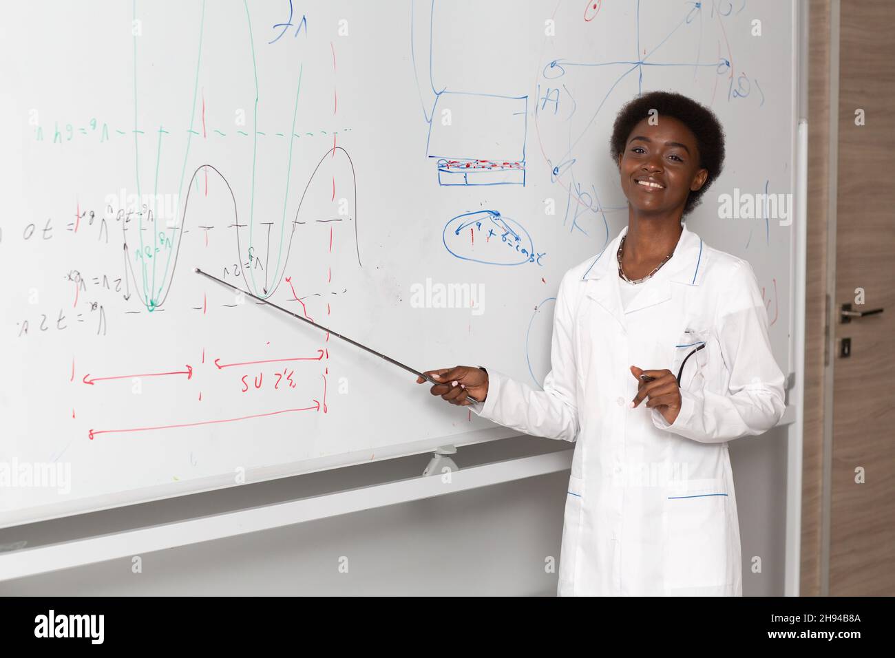 African American smiling woman math teacher stands at black board with ...