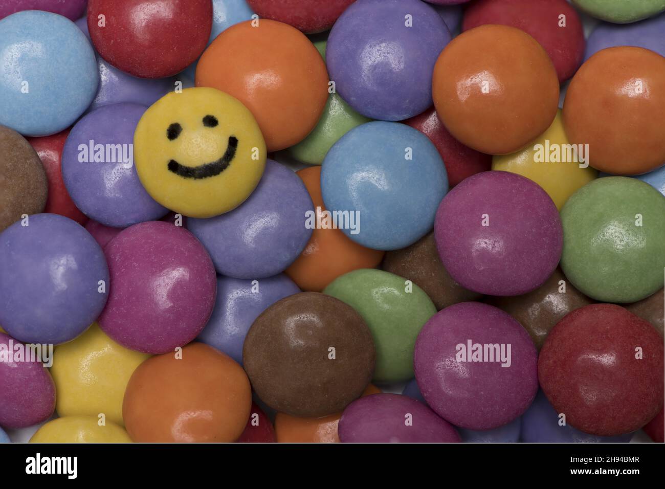 a yellow smiley between colorful round sweets in different colors lying ...