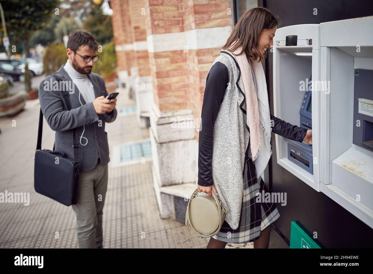 A young attractive woman is using ATM machine on the street in a ...