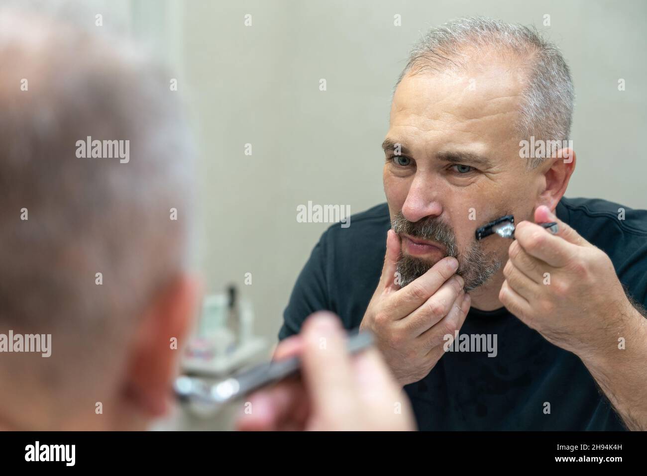 Serious handsome man looking in mirror and shaving his whiskers Stock ...