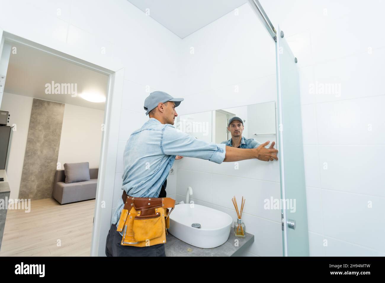 Handyman installing mirror in bathroom Stock Photo - Alamy