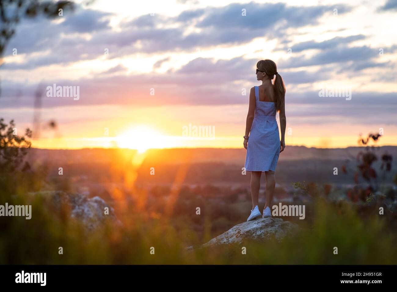 Dark silhouette of a young woman standing on a stone enjoying sunset ...
