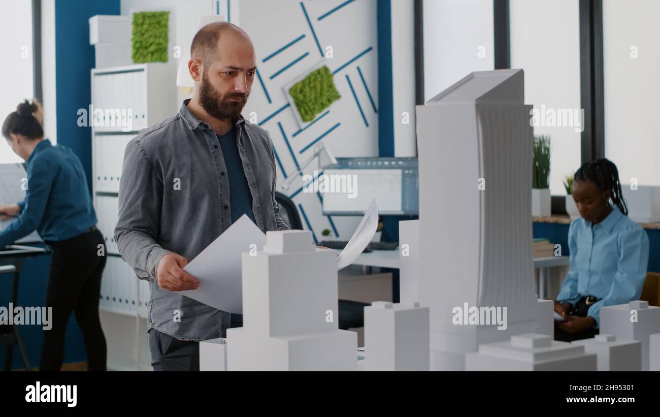 Portrait Of Engineer Analyzing Blueprints Plan And Building Model To Design Architectural