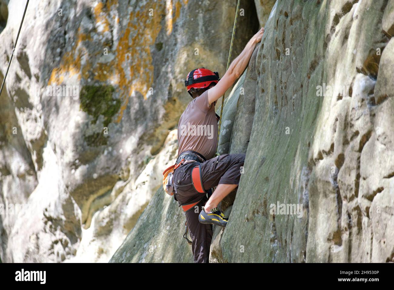 Young man climbing steep wall of rocky mountain. Male climber overcomes ...