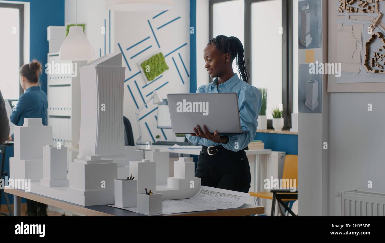 Woman architect holding laptop to analyze building model in ...