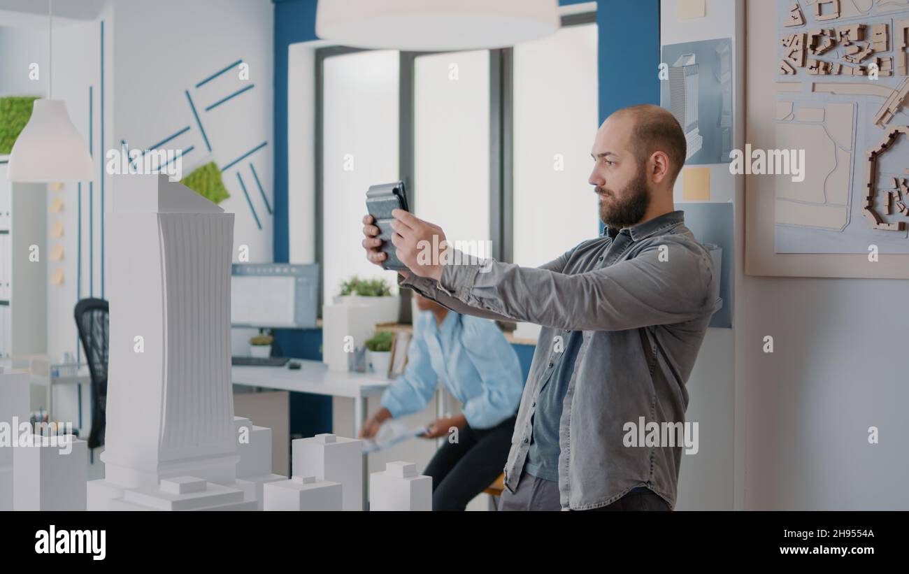Architect Analyzing Building Model On Digital Tablet To Plan Blueprints For Construction Layout