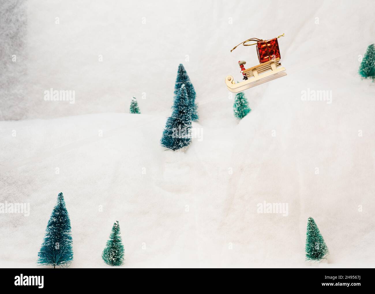 Miniature Santa Claus slides on a ski slope with his sledge on a white ...