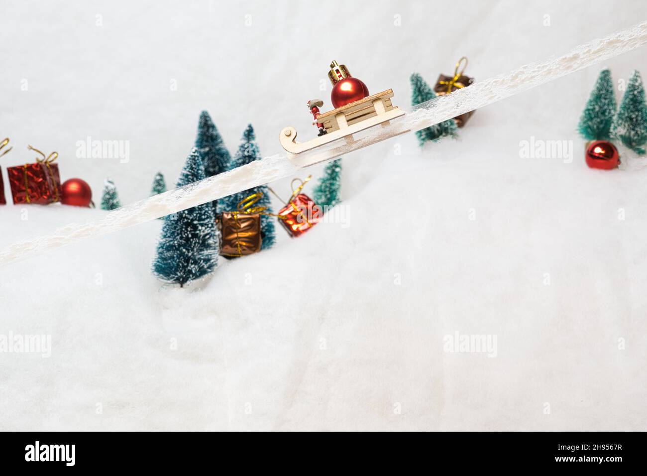 Miniature Santa Claus slides on a ski slope with his sledge on a white ...