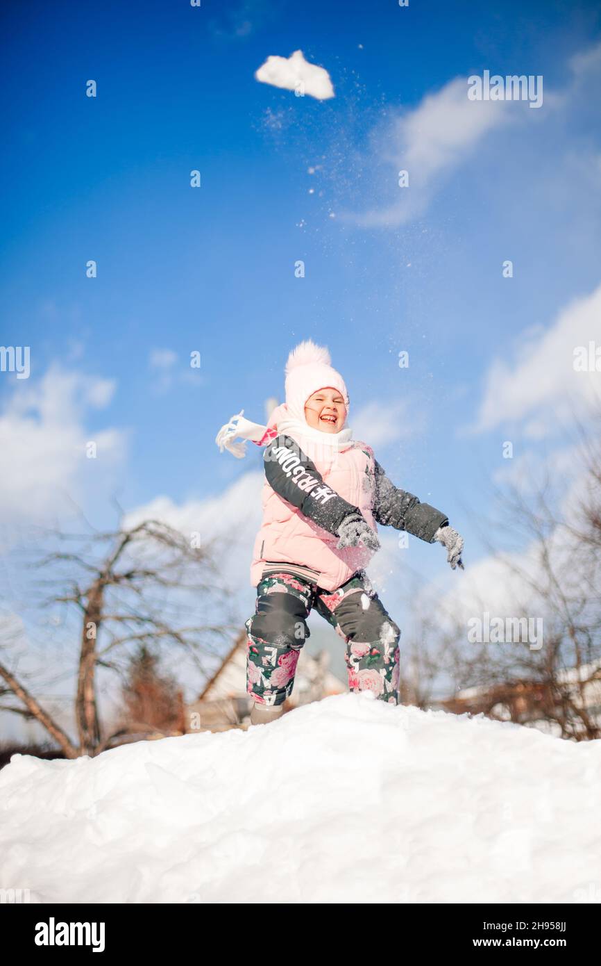 Child throws snowballs in winter park. Little girl in pink winter suit ...