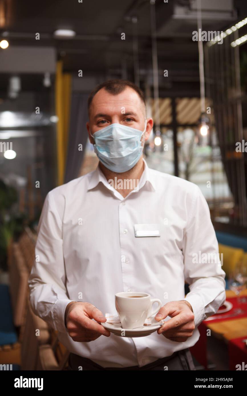 Vertical shot of a male waiter wearing medical face mask, working ...