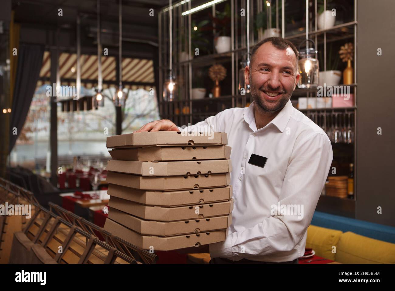 Cheerful waiter smiling, carrying many pizza boxes ready for delivery ...