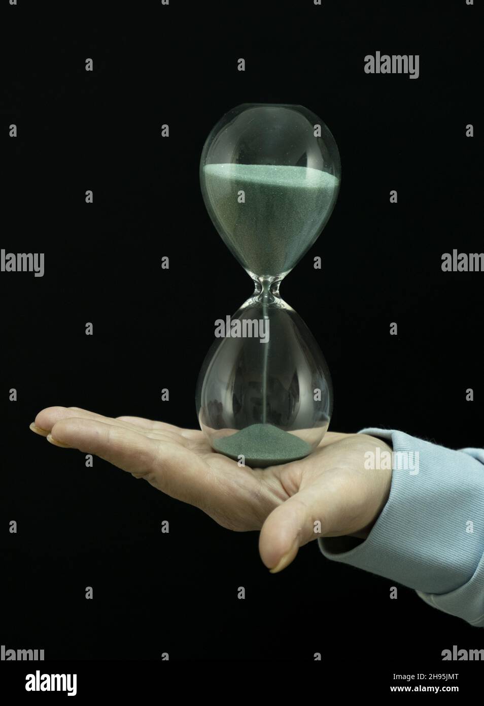 Vertical shot of a person holding an hourglass on a black background ...