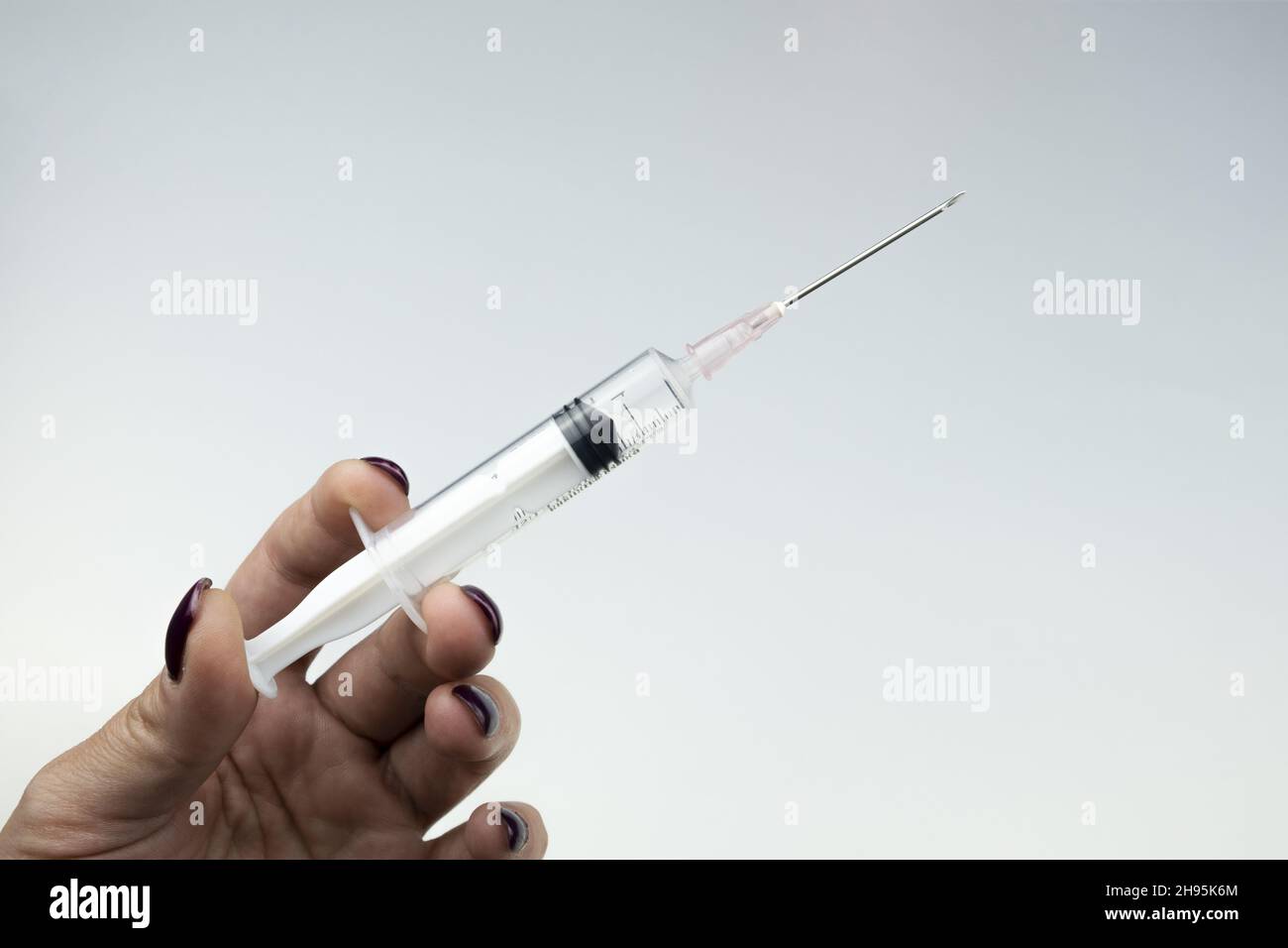 Closeup of a nurse's hand holding a syringe against a white background ...