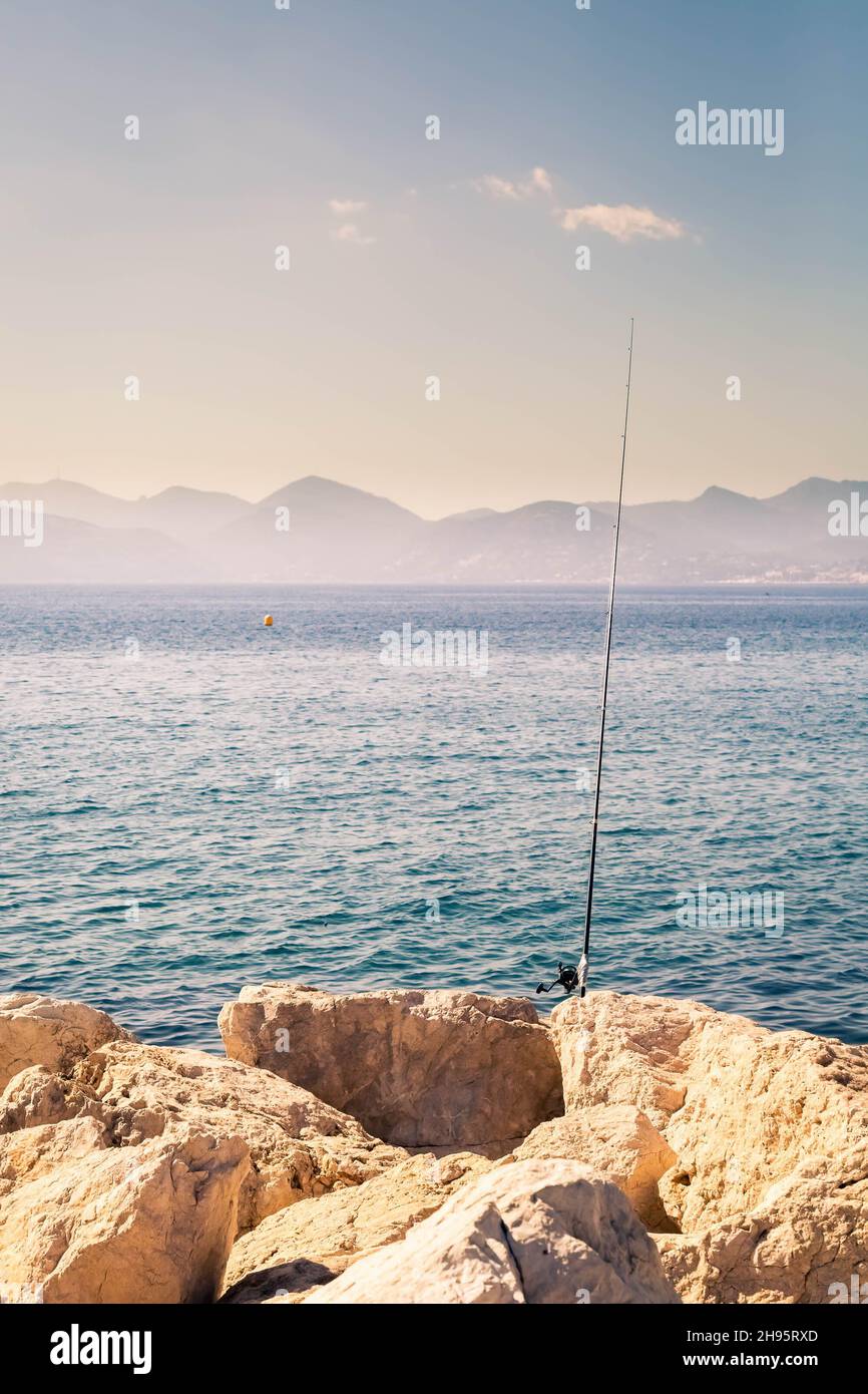 Fishing rod stuck onto rocky dock with mountains in a hazy distance ...