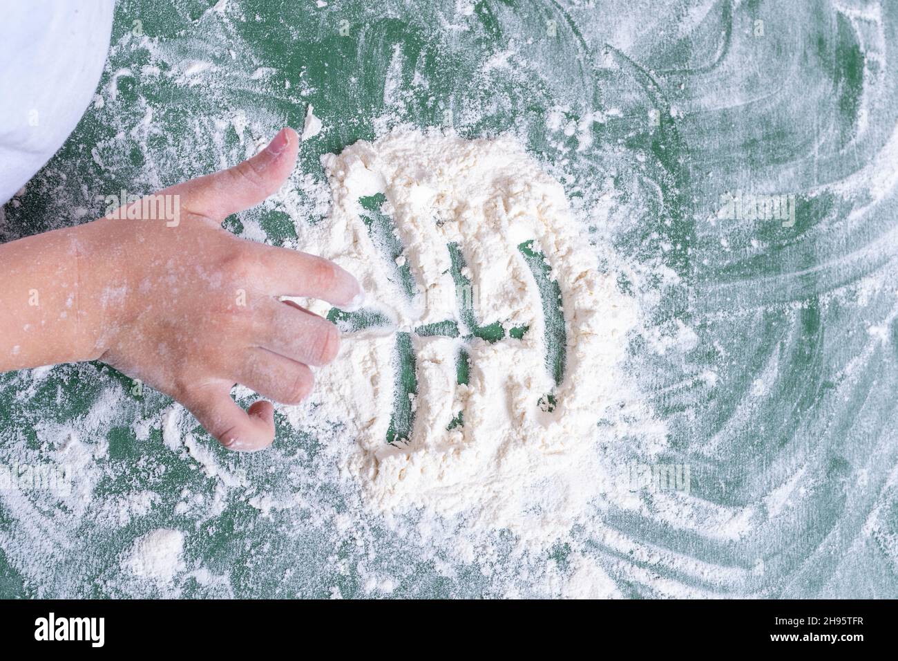 Children's hand drawing a tree on flour on the table. The child plays ...