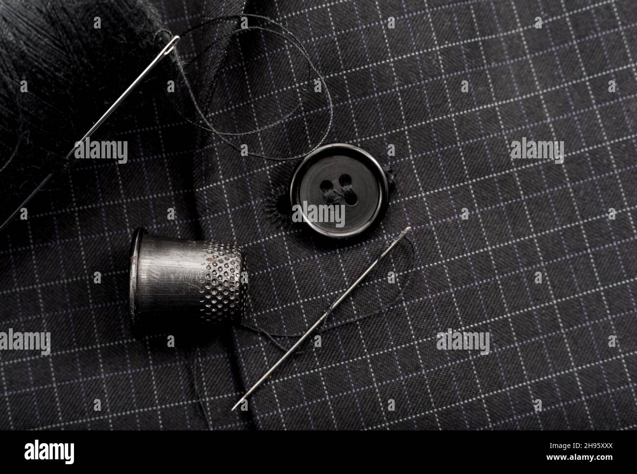 A needle and thread sews up a button on a plaid suit. Thimble. Textile ...