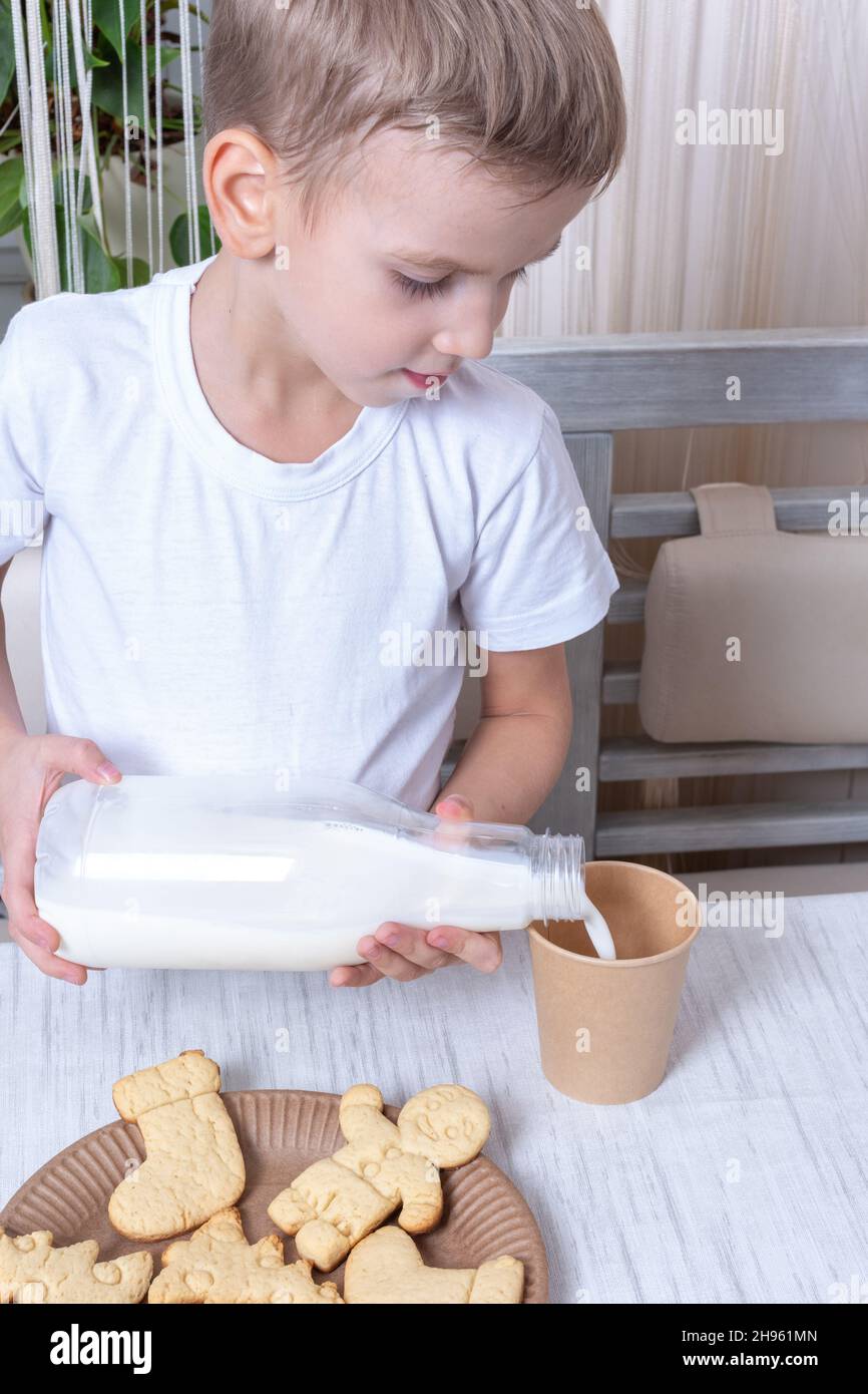 Cute caucasian boy pours milk into a craft paper cup on the table next ...