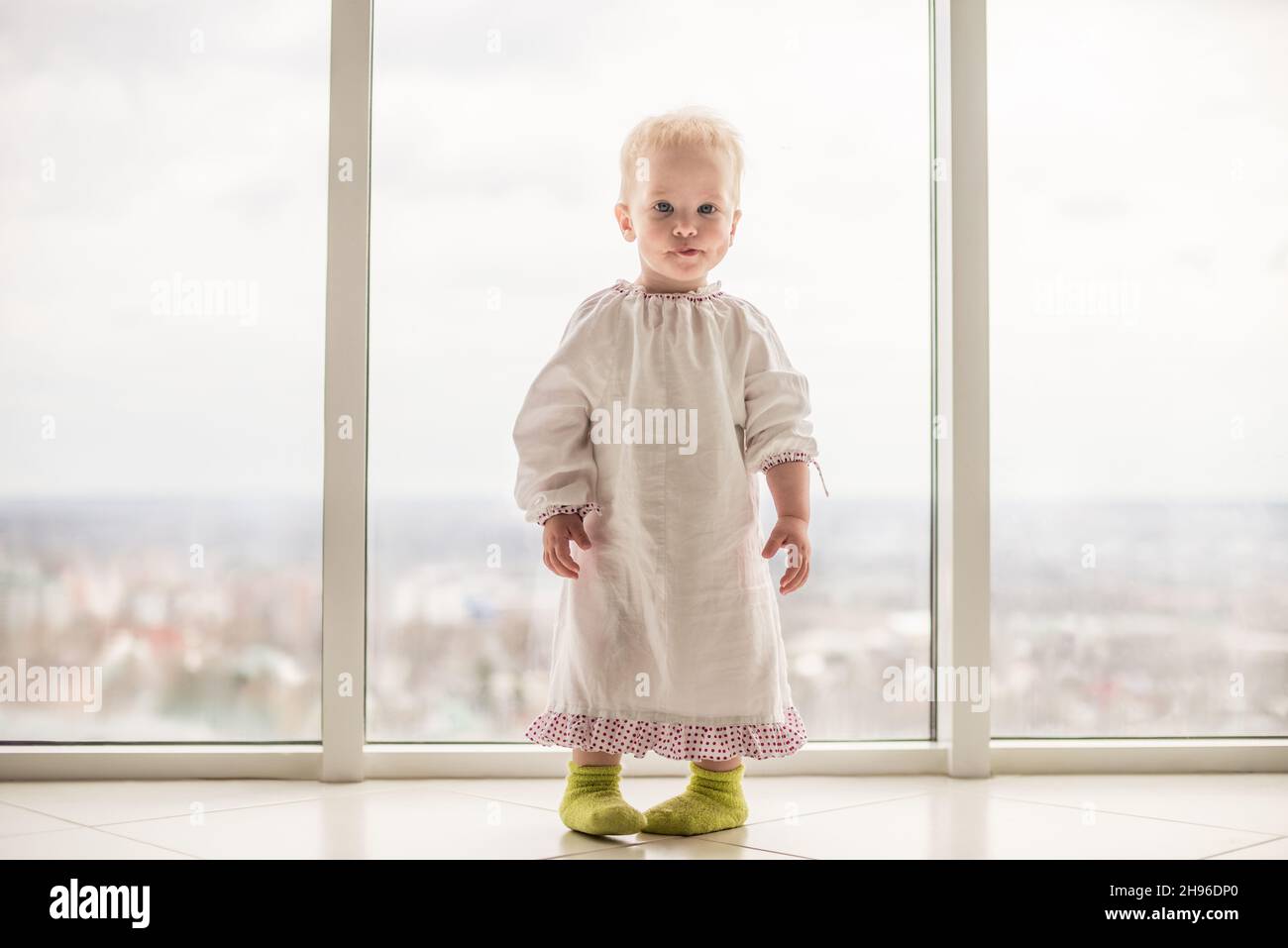 Beautiful little girl is standing at the window and smiling Stock Photo ...