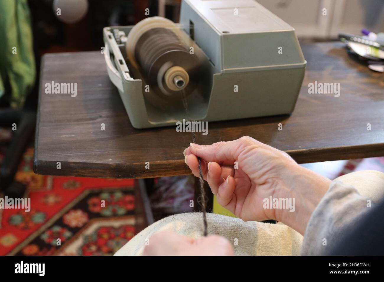 A woman makes yarn for knitting with an electric spinning wheel Stock ...
