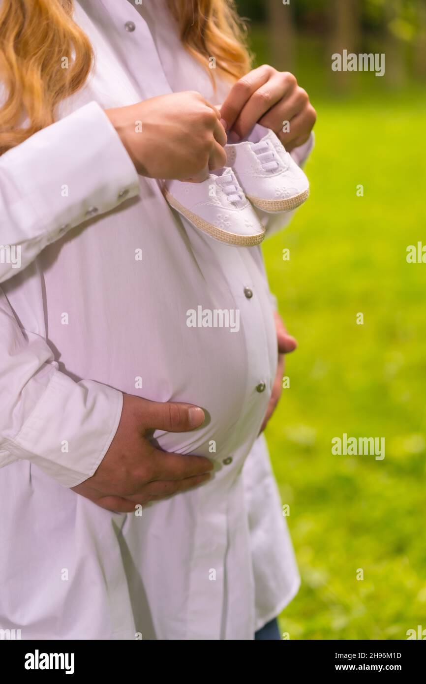Vertical shot of a pregnant female posing holding boots for the baby ...