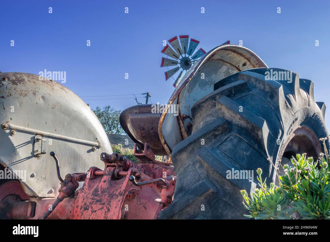 A detail of antique tractor with an old windmill in the background in ...
