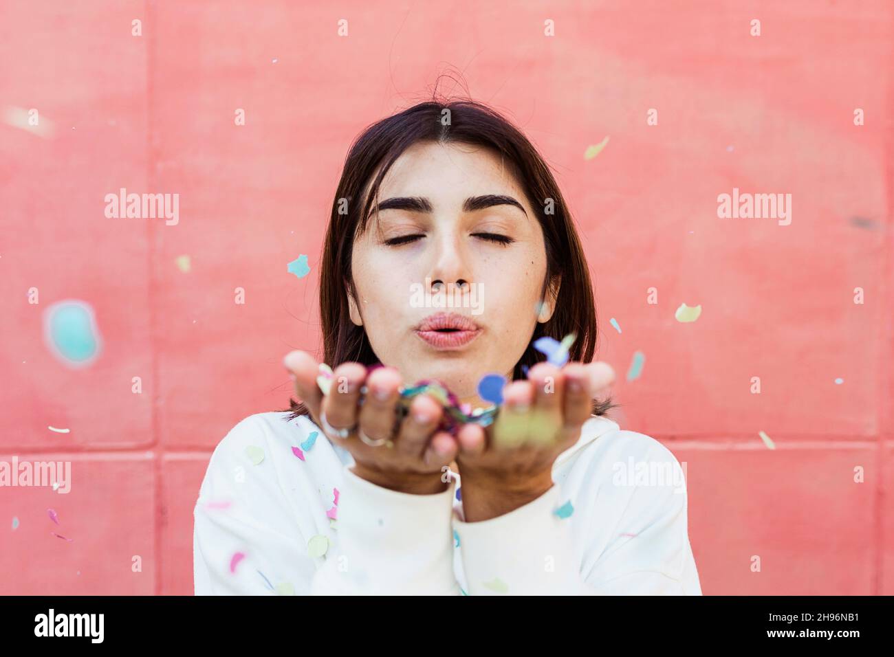 Beautiful hispanic young woman blowing confetti with pink background ...